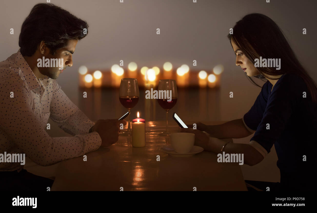 Couple using mobile phone while having dinner in restaurant at night ...