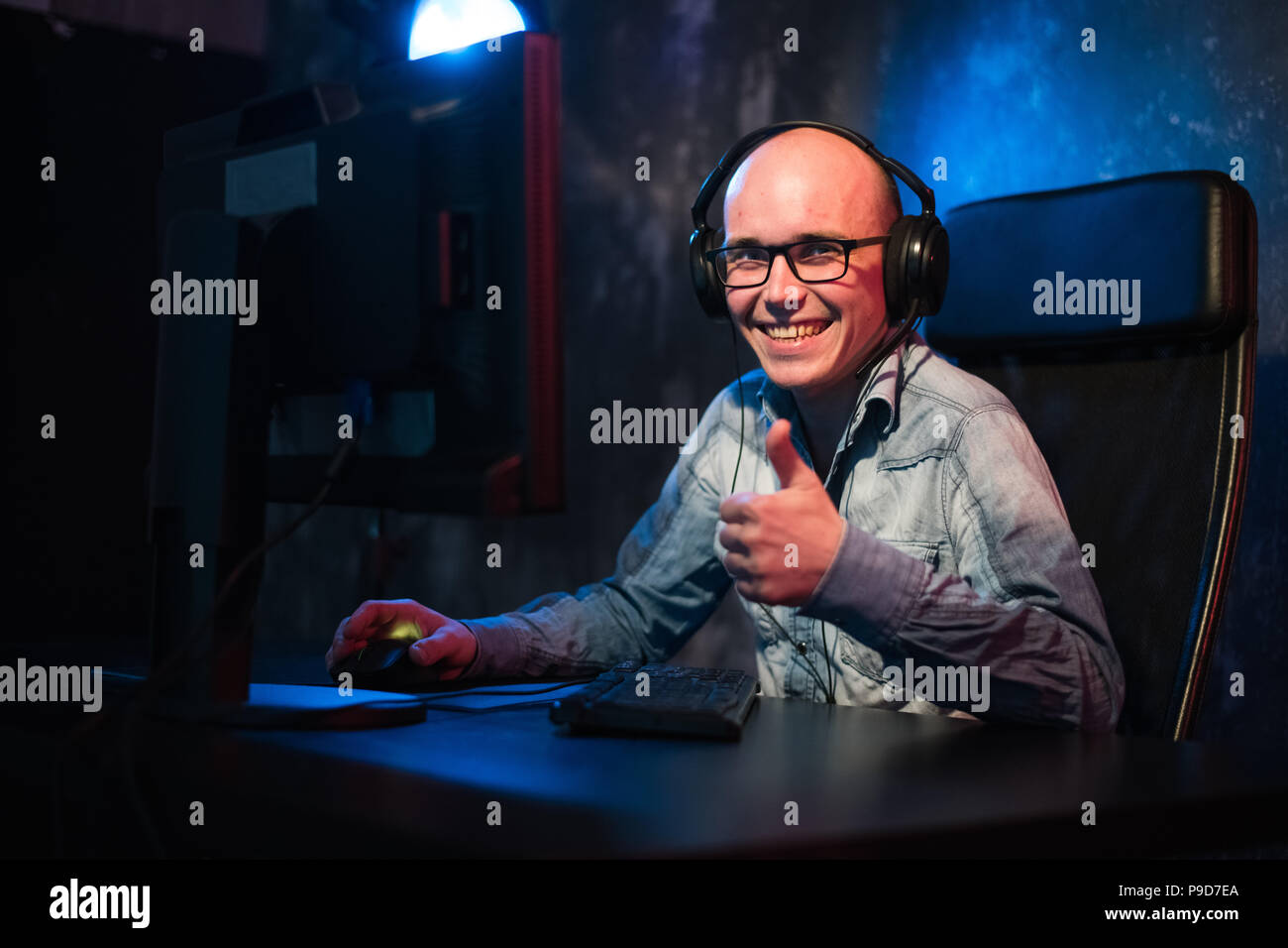 Adult gamer sits at home with a computer, shows a thumbs up and looks ...