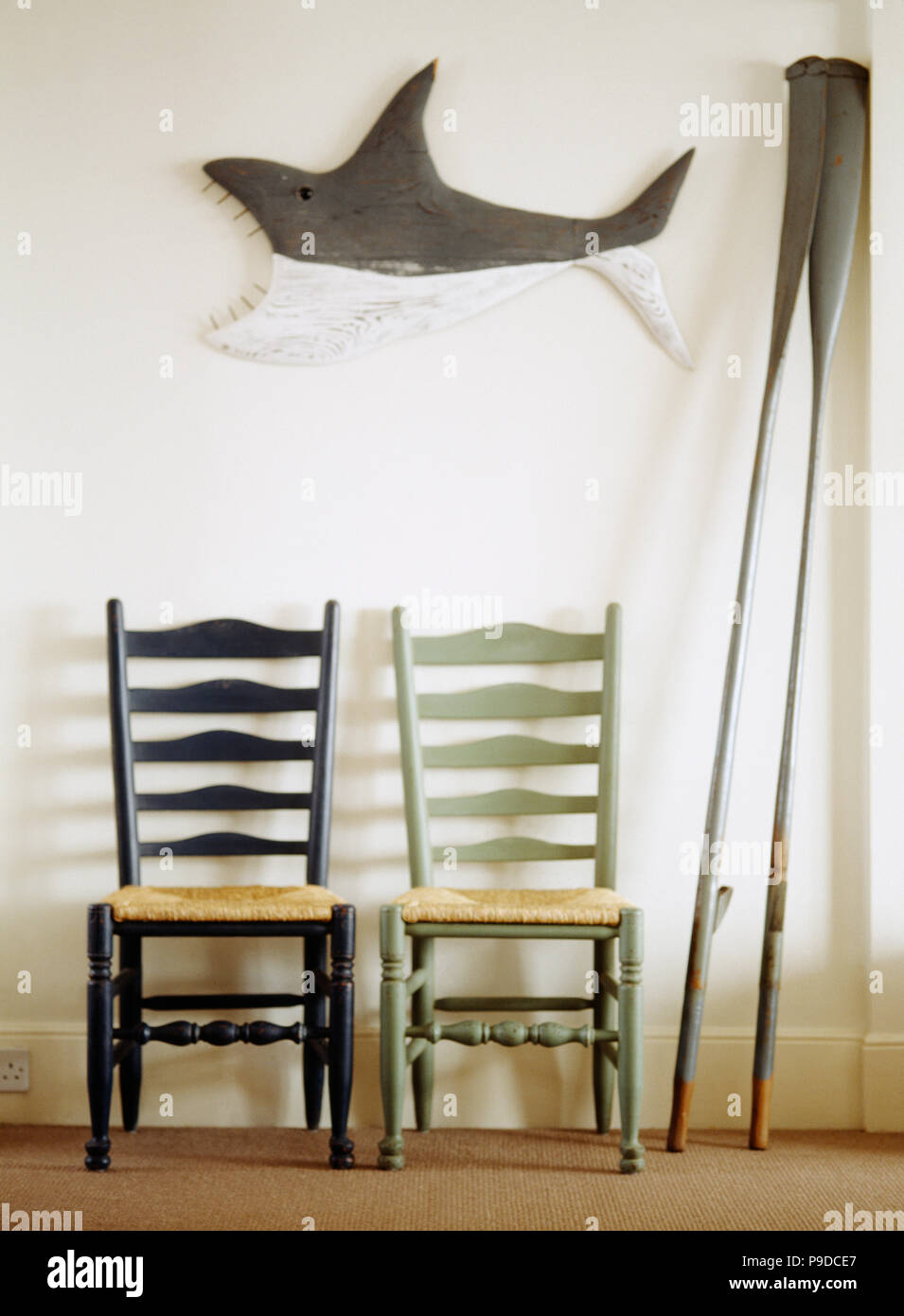 Large wooden fish above rush-seated ladderback chairs and pair of oars ...