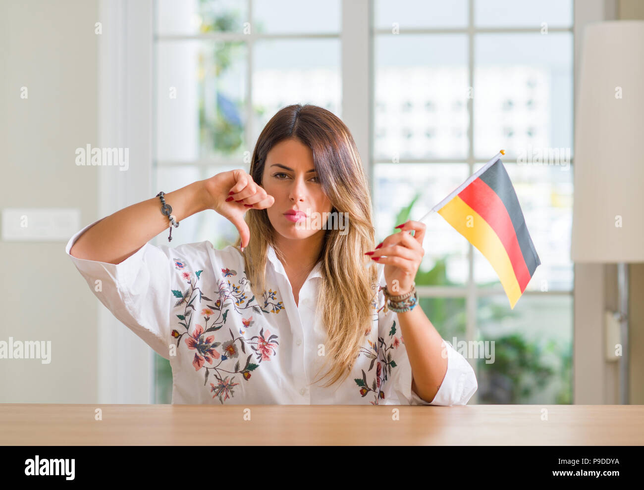 Young woman at home holding flag of Germany with angry face, negative ...