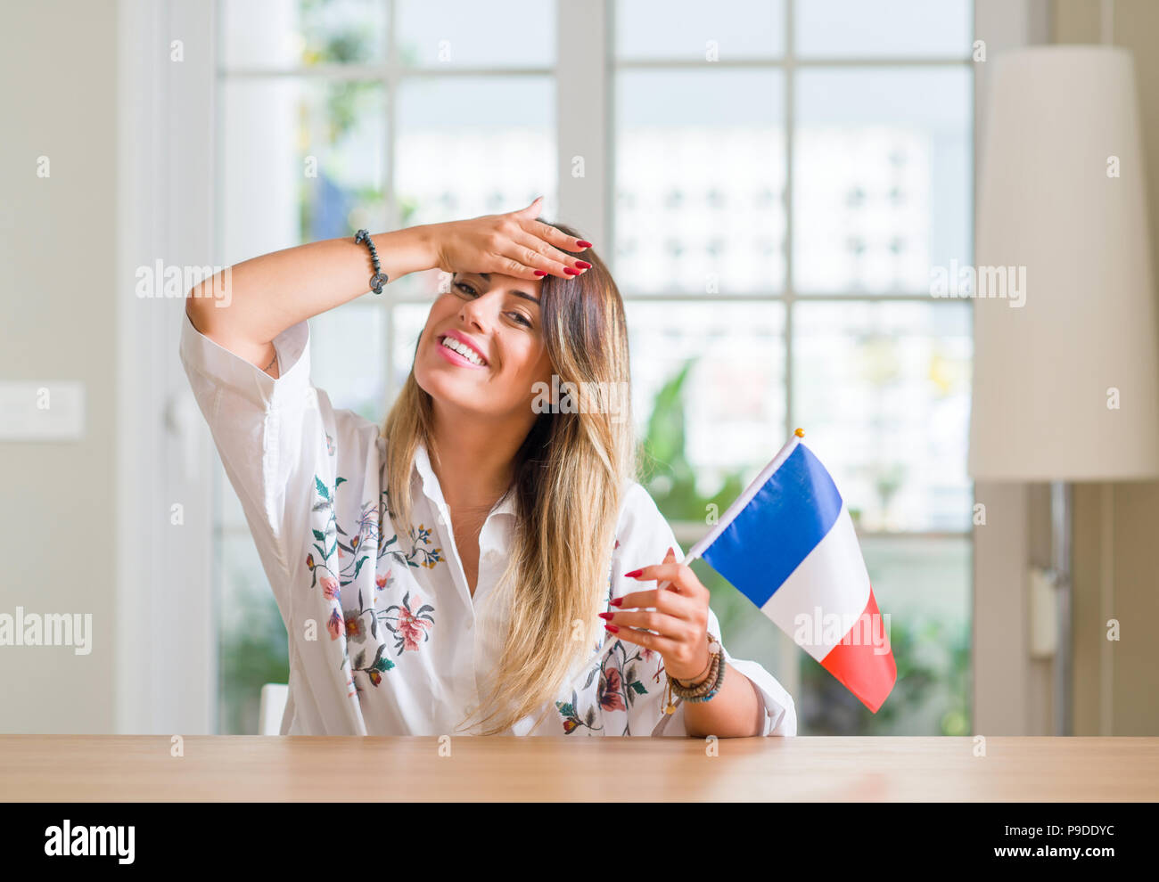 Young woman at home holding flag of France stressed with hand on head ...