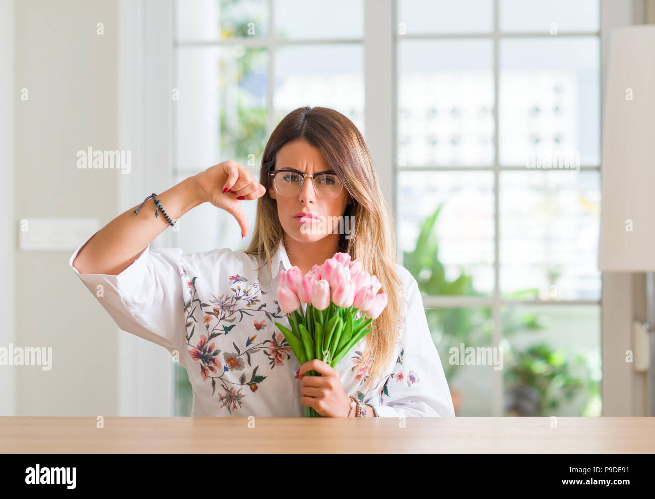 Young woman at home holding pink tulips flowers with angry face ...
