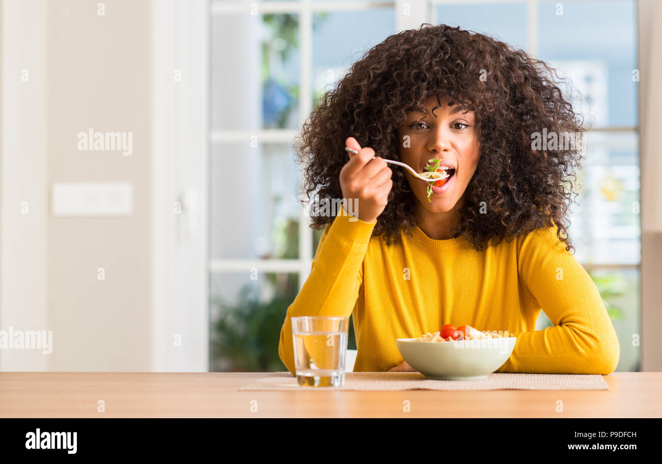 African american woman eating pasta salad at home with a confident ...