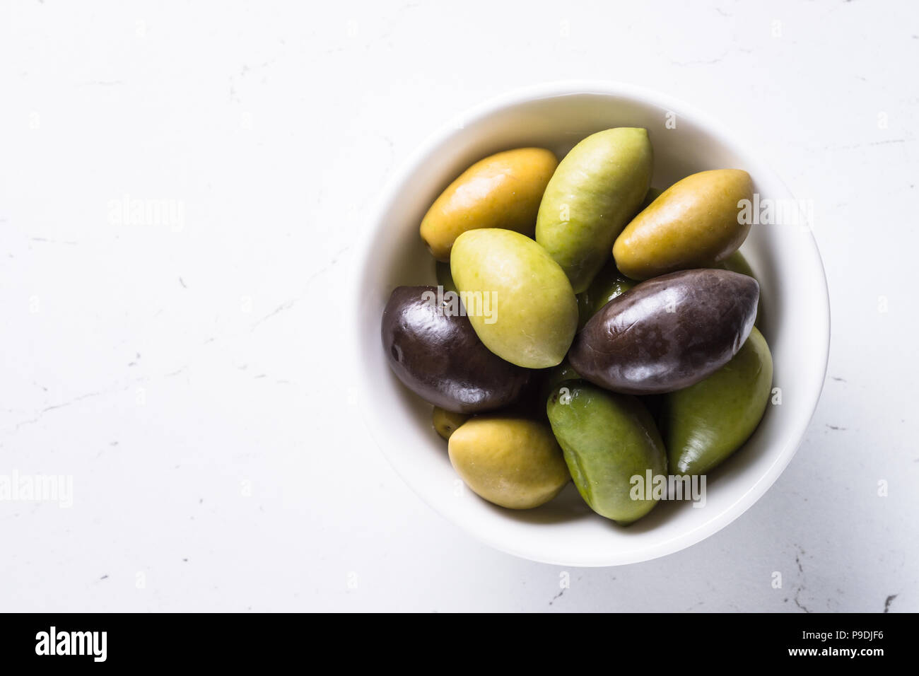 Black and green olives in a bowl on white marble table. Top view with ...