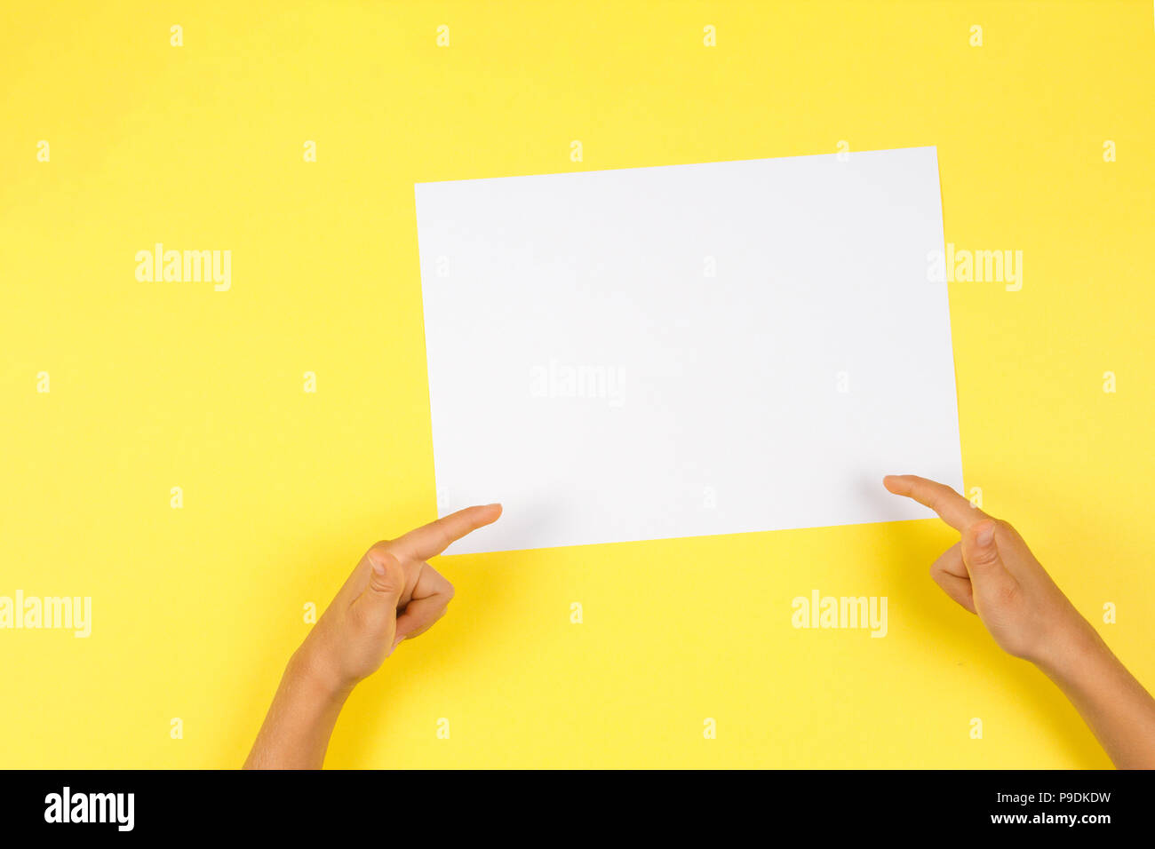 Kids hands fingers pointing to white blank paper card on yellow ...