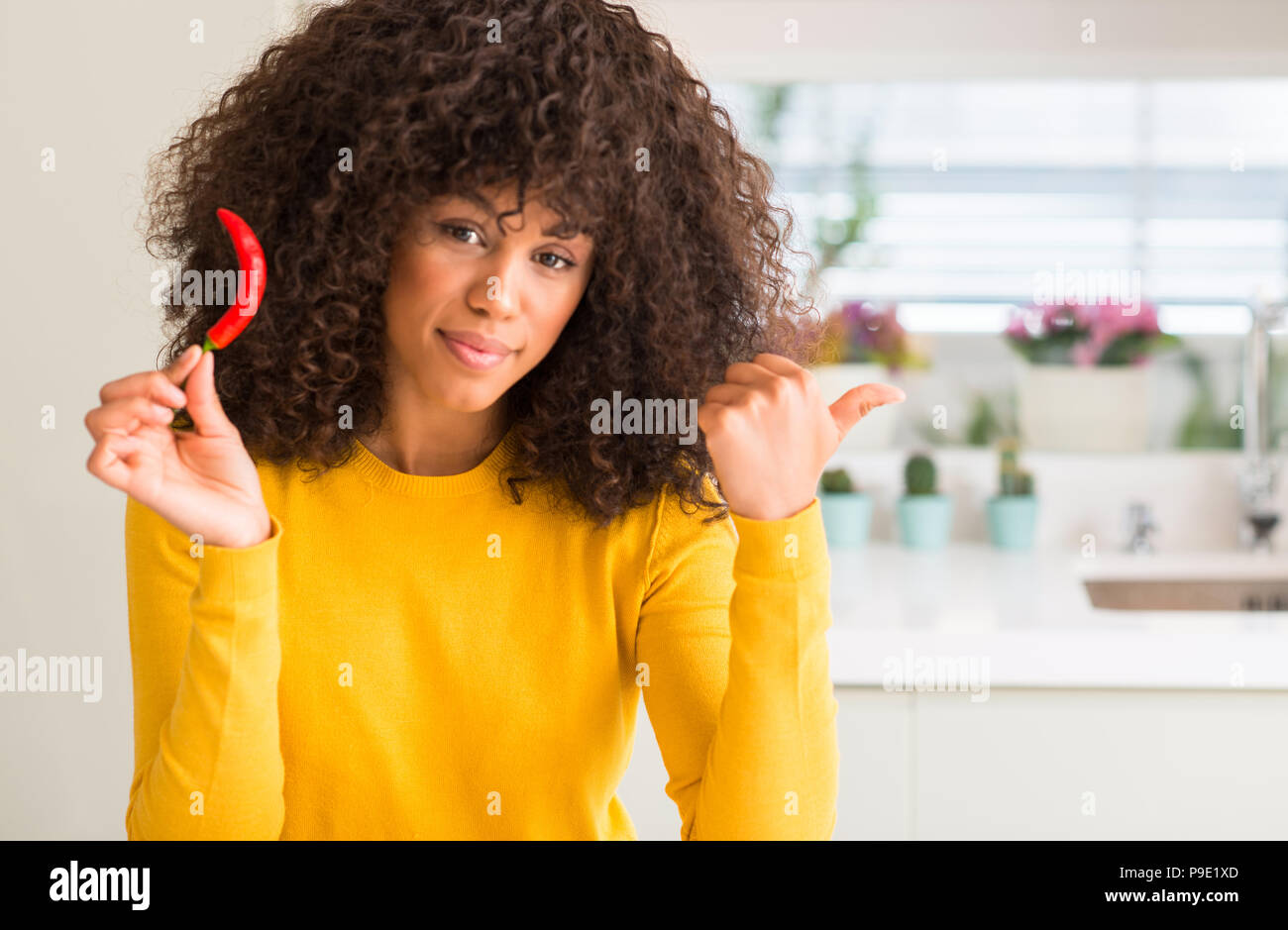 African american woman eating red hot chili pepper pointing with hand ... African american woman eating red hot chili pepper pointing with hand ...