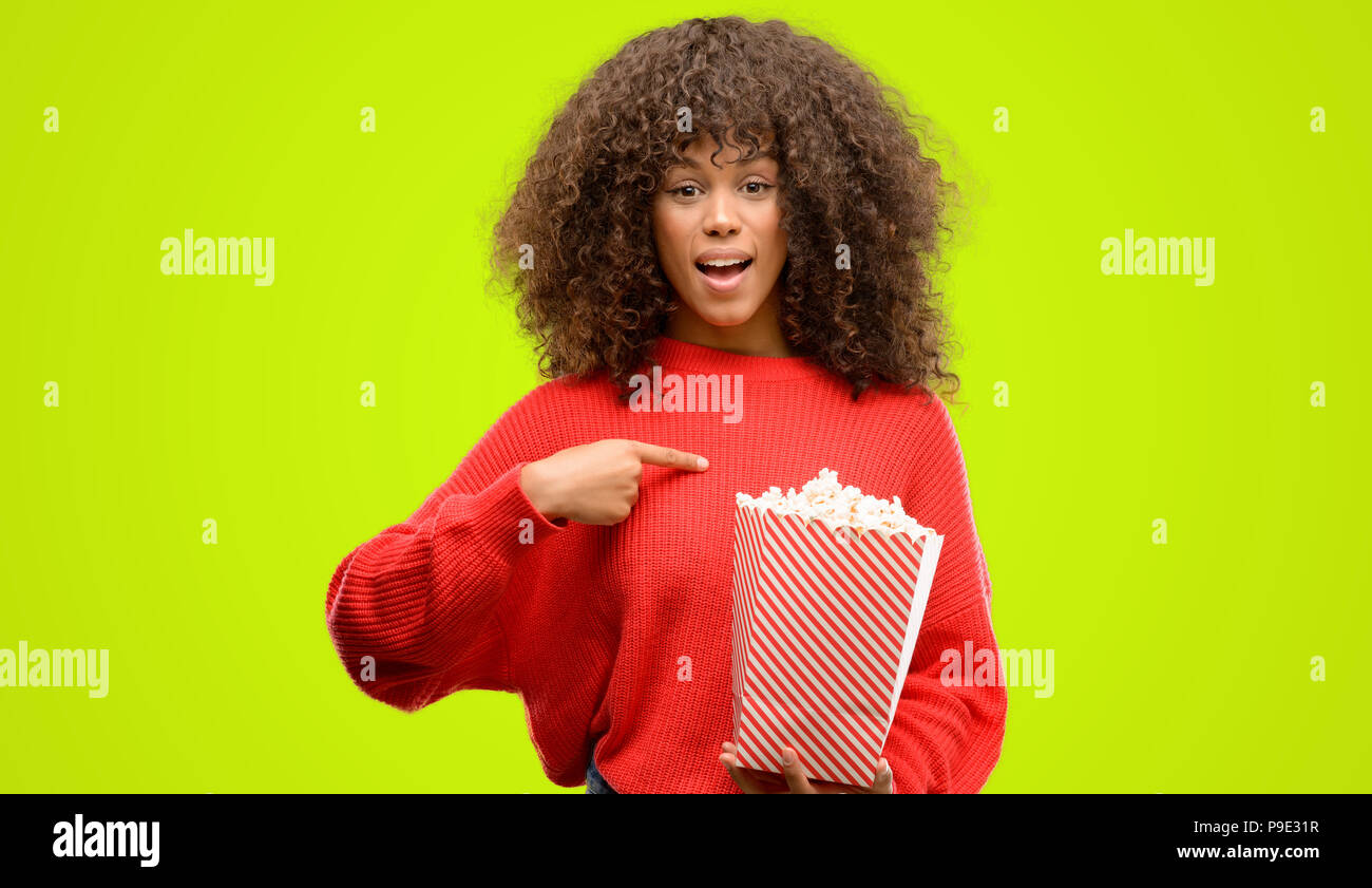 African american woman eating popcorn with surprise face pointing ...