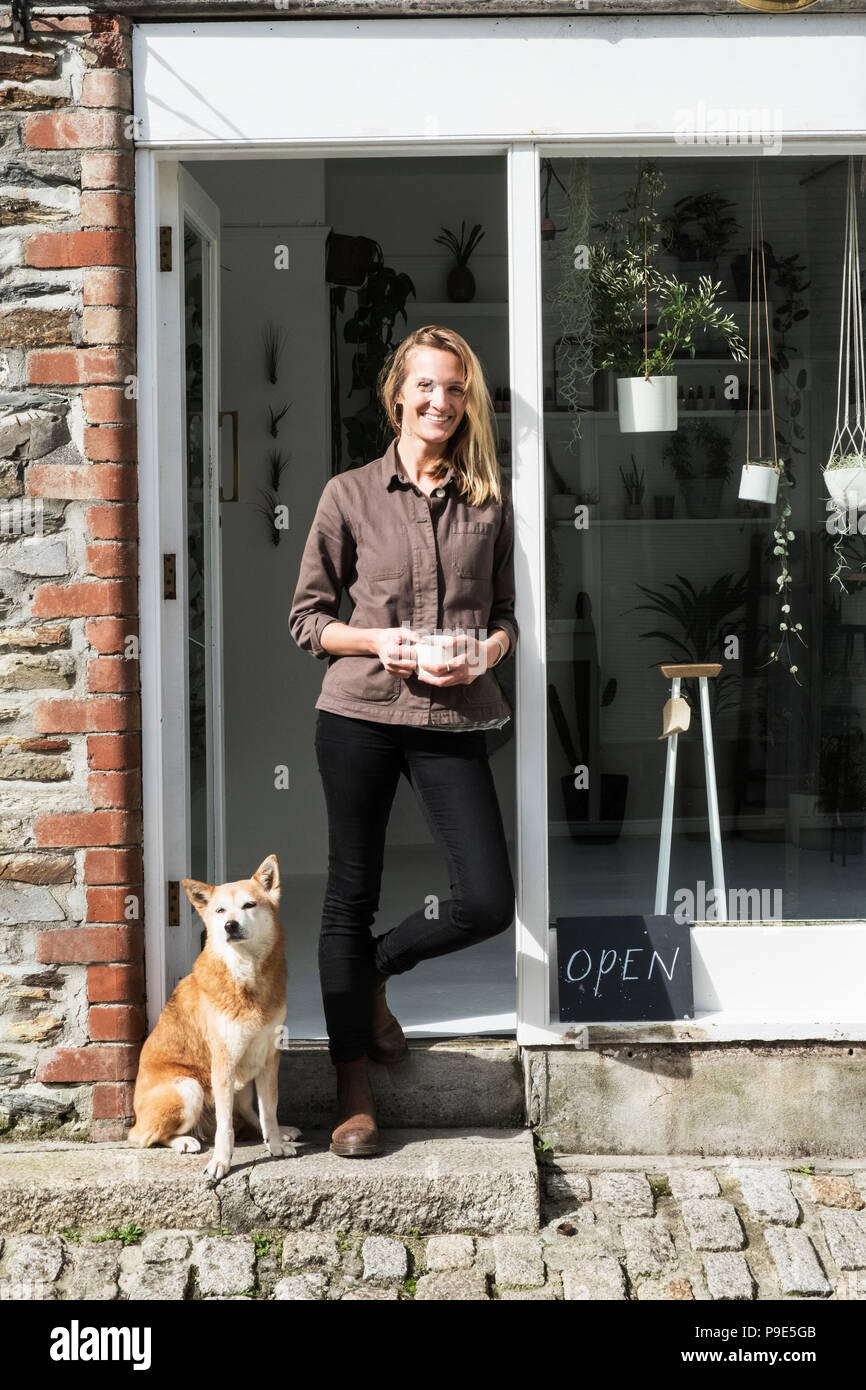 Smiling female owner of plant shop standing outside her store, a dog ...