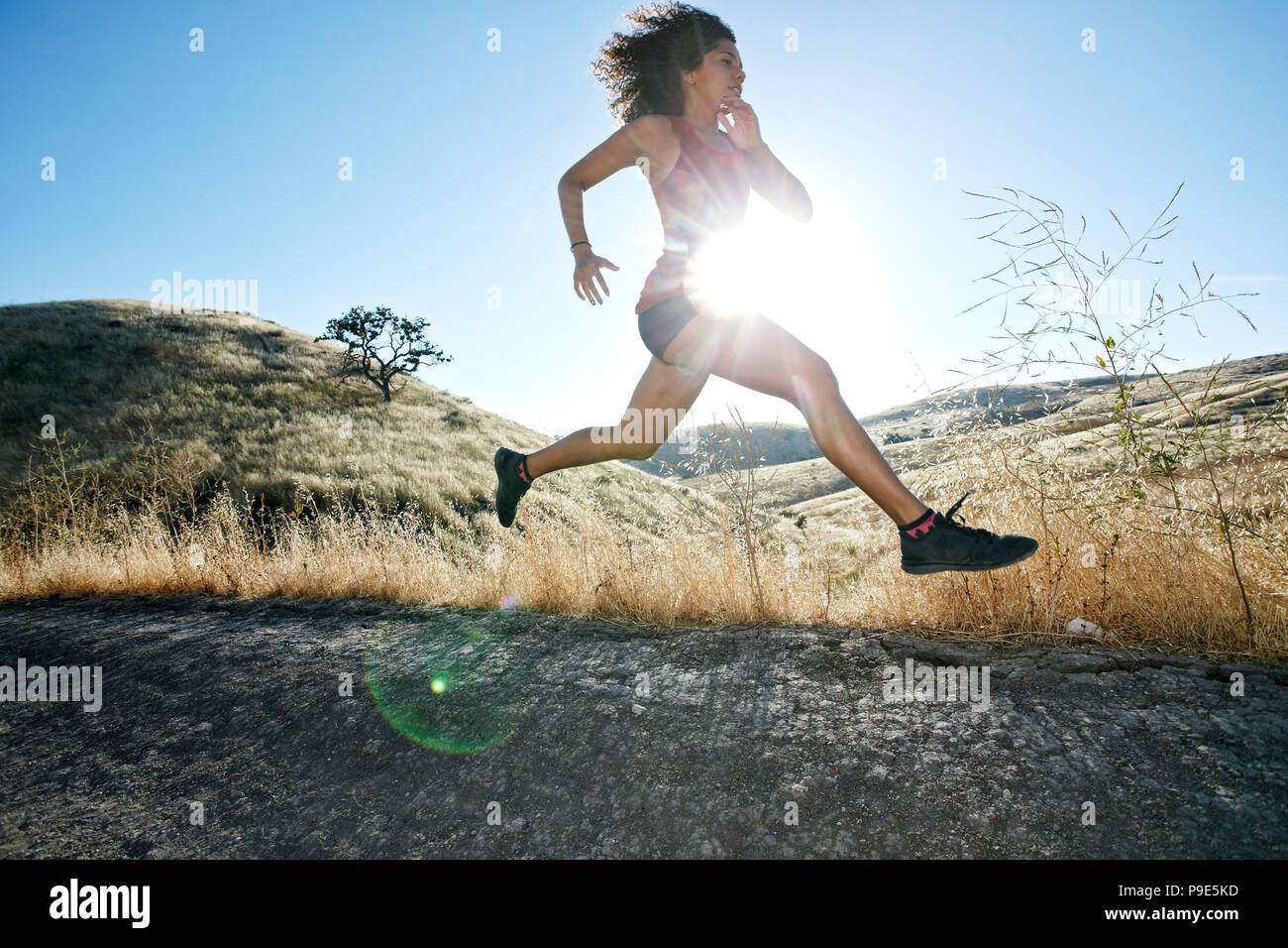 Young woman with curly brown hair running in urban park Stock Photo - Alamy