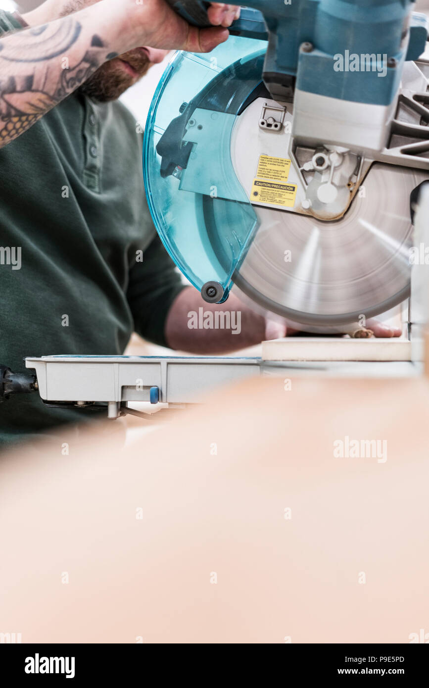 Carpenter using a radial saw to cut a wooden board in a woodworking ...