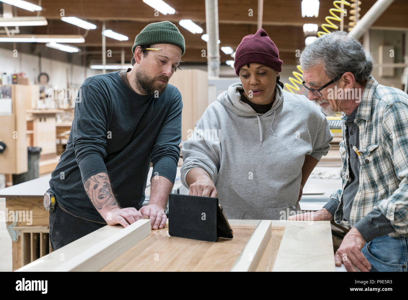 A group of mixed race carpenters discussing a project at a work station ...