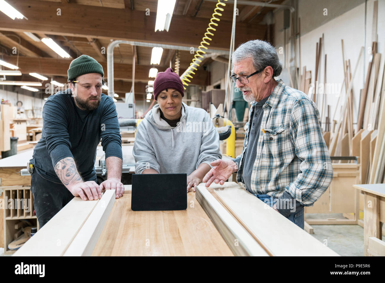 A group of mixed race carpenters discussing a project at a work station ...