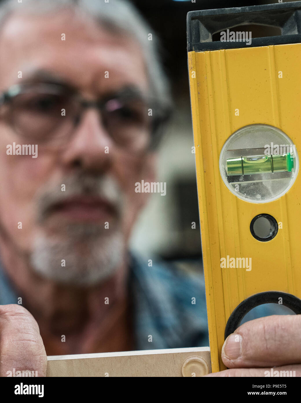 A senior man with glasses and beard in a woodworkers shop, using a ...