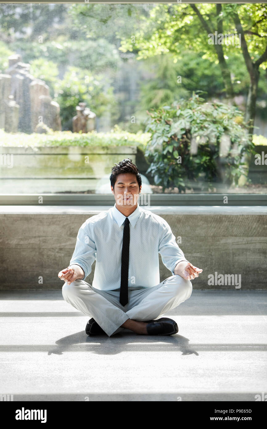 A businessman taking a meditative break in a room full of indoor plants ...