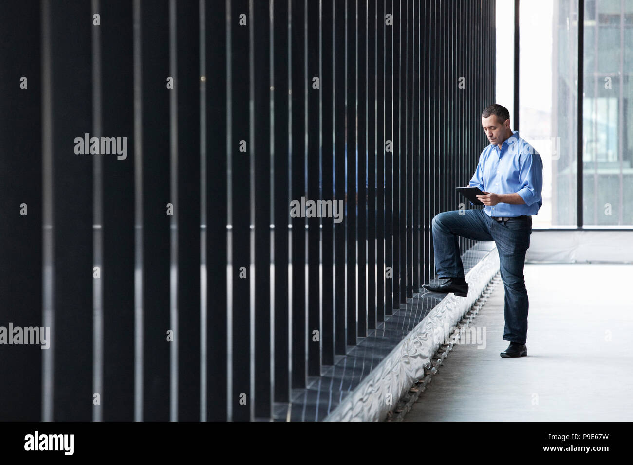 A Caucasian male architect standing by a wall of windows, using a ...