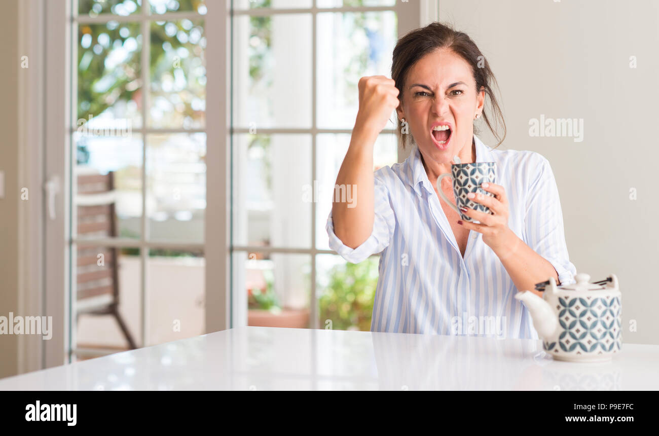 Middle aged woman drinking a cup of tea or coffee annoyed and ...