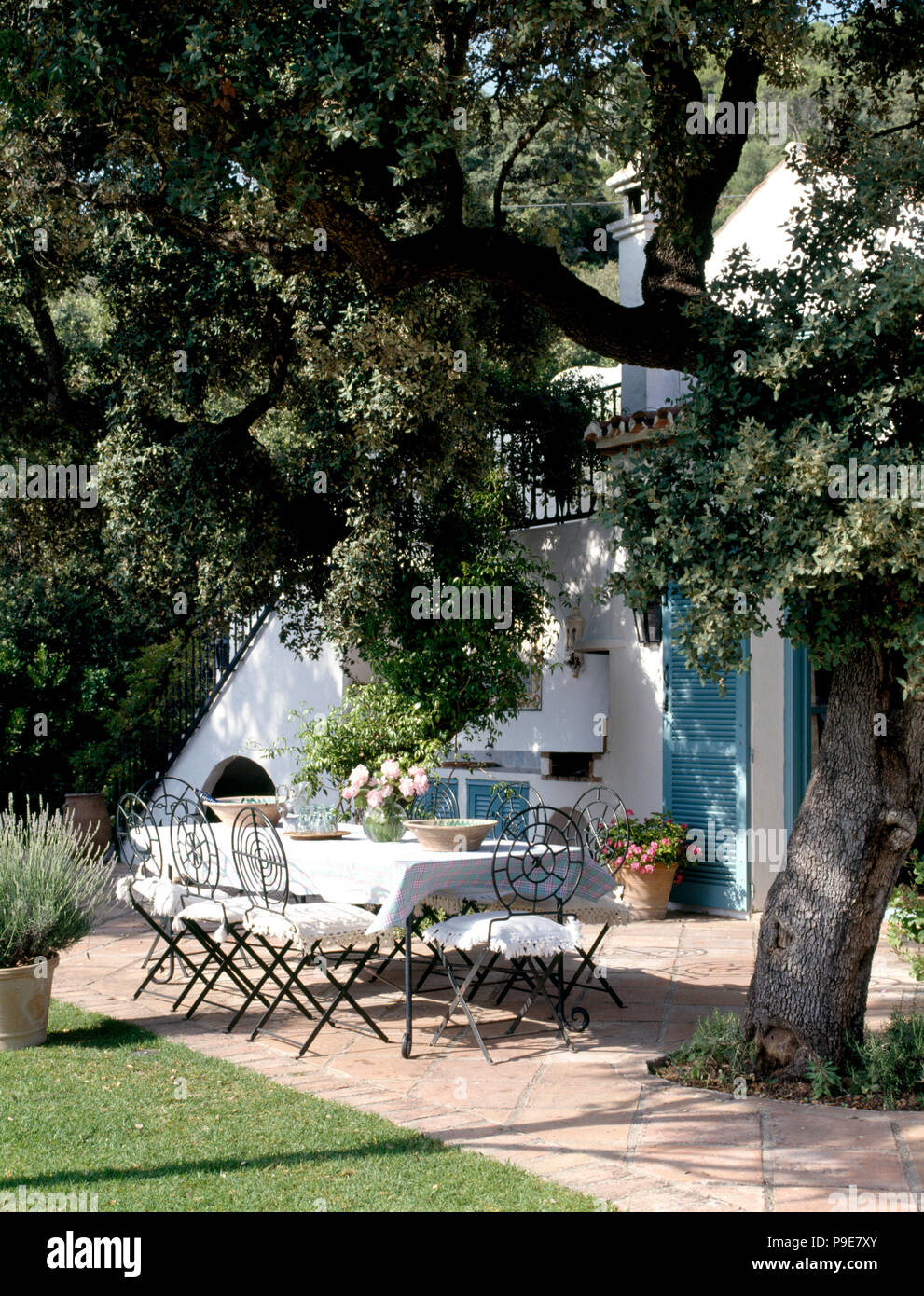 Tall tree beside Spanish terrace with metal chairs at table with a ...