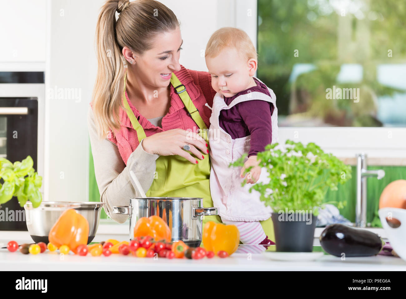 Mother working in kitchen while carrying child Stock Photo - Alamy