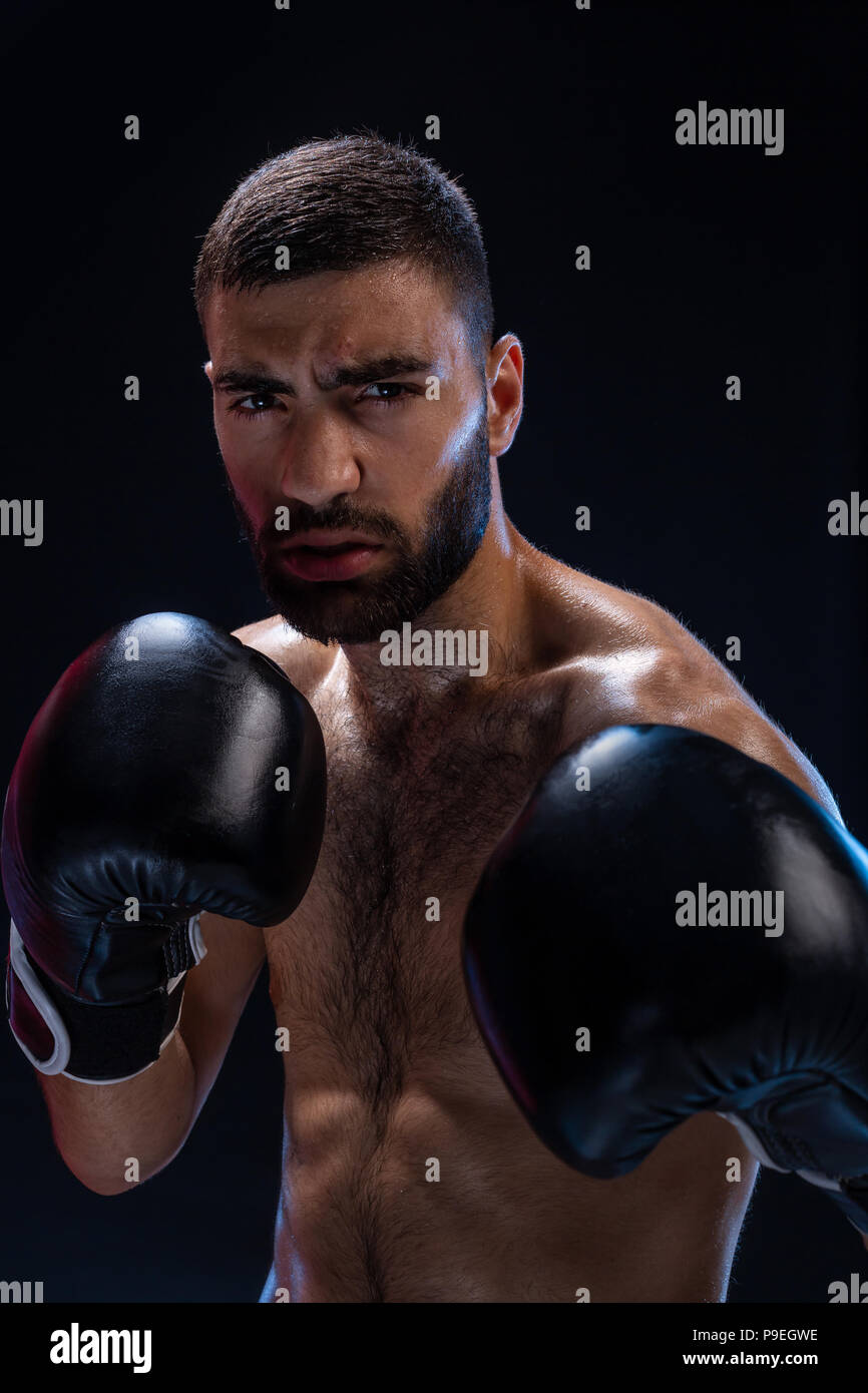 Portrait of tough male boxer posing in boxing stance against black ...