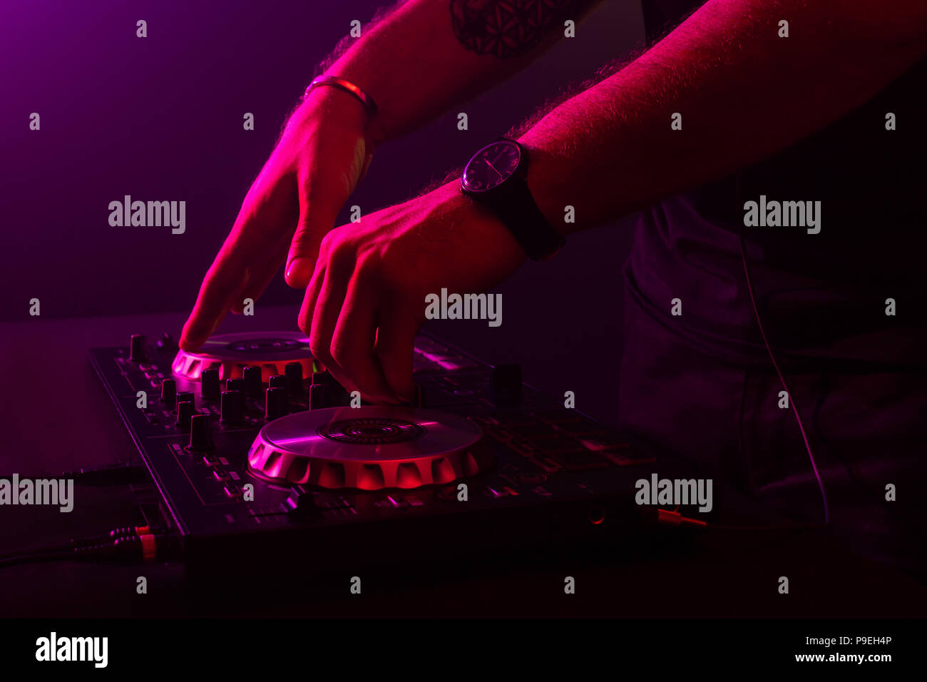 Dj mixing on turntables with color light effects. Soft focus on hand ...