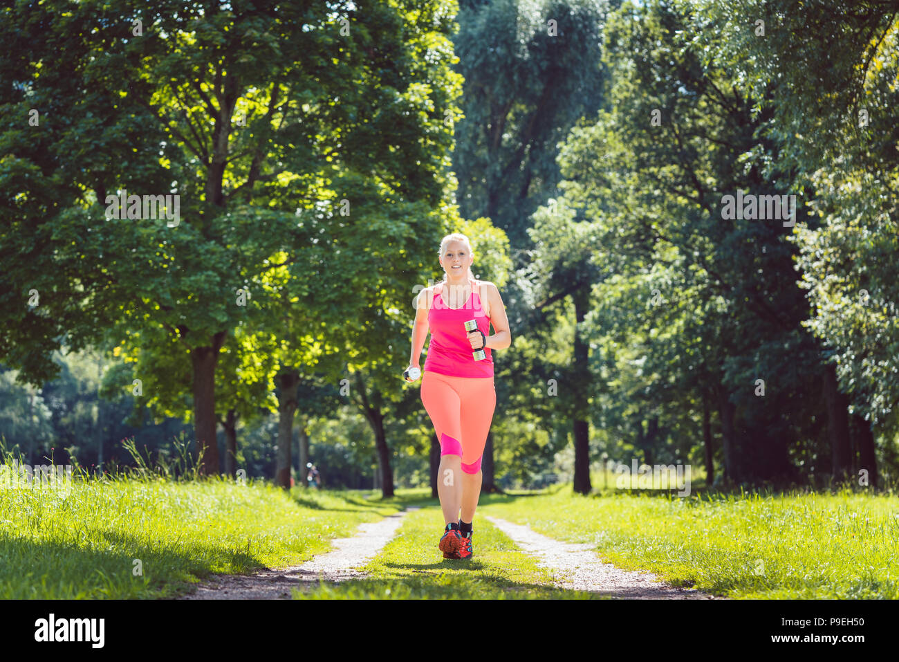 Woman running down a path on meadow with weight dumbbells Stock Photo ...