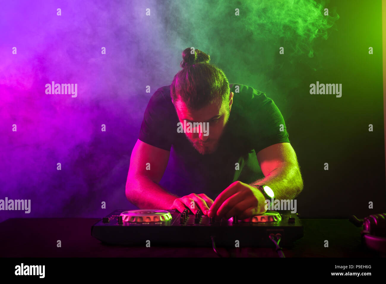Attractive young DJ playing on turntables with color light effects ...