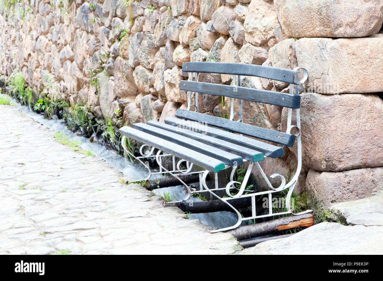 Wooden bench over a narrow water channel by a stone wall and ...