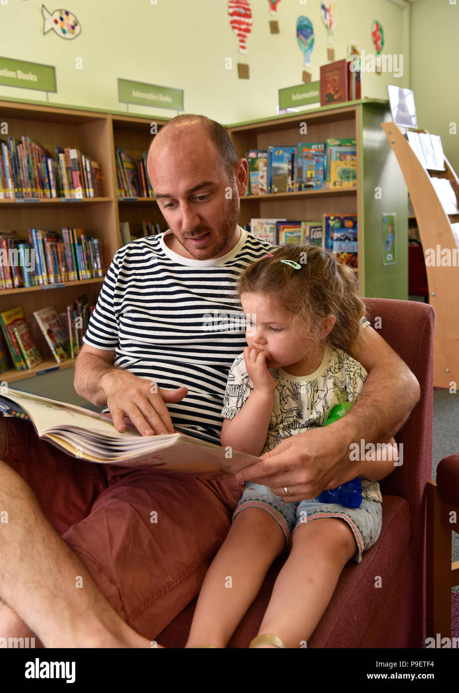 Father reading to his daughter in children's library, Haslemere, Surrey ...