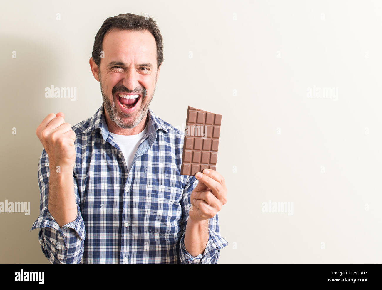 Senior man eating chocolate bar screaming proud and celebrating victory ...
