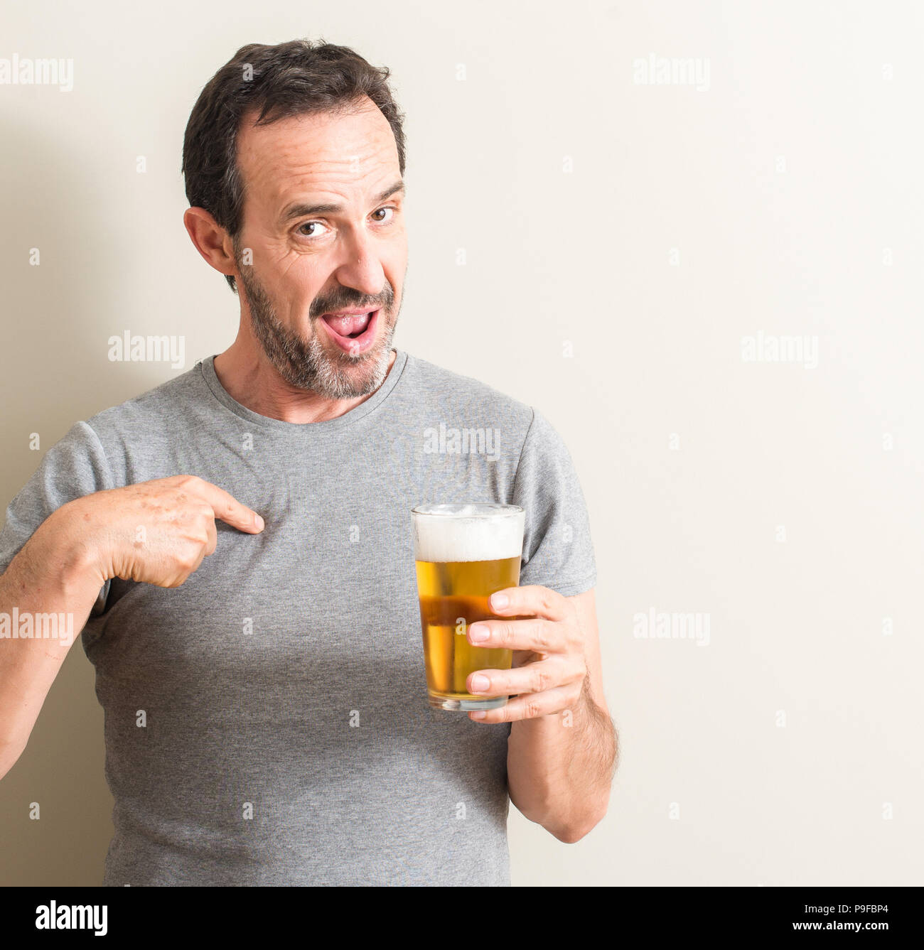 Senior man drinking beer with surprise face pointing finger to himself ...