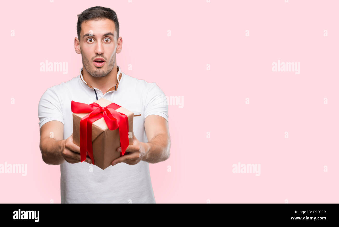 Handsome young man giving a present scared in shock with a surprise ...