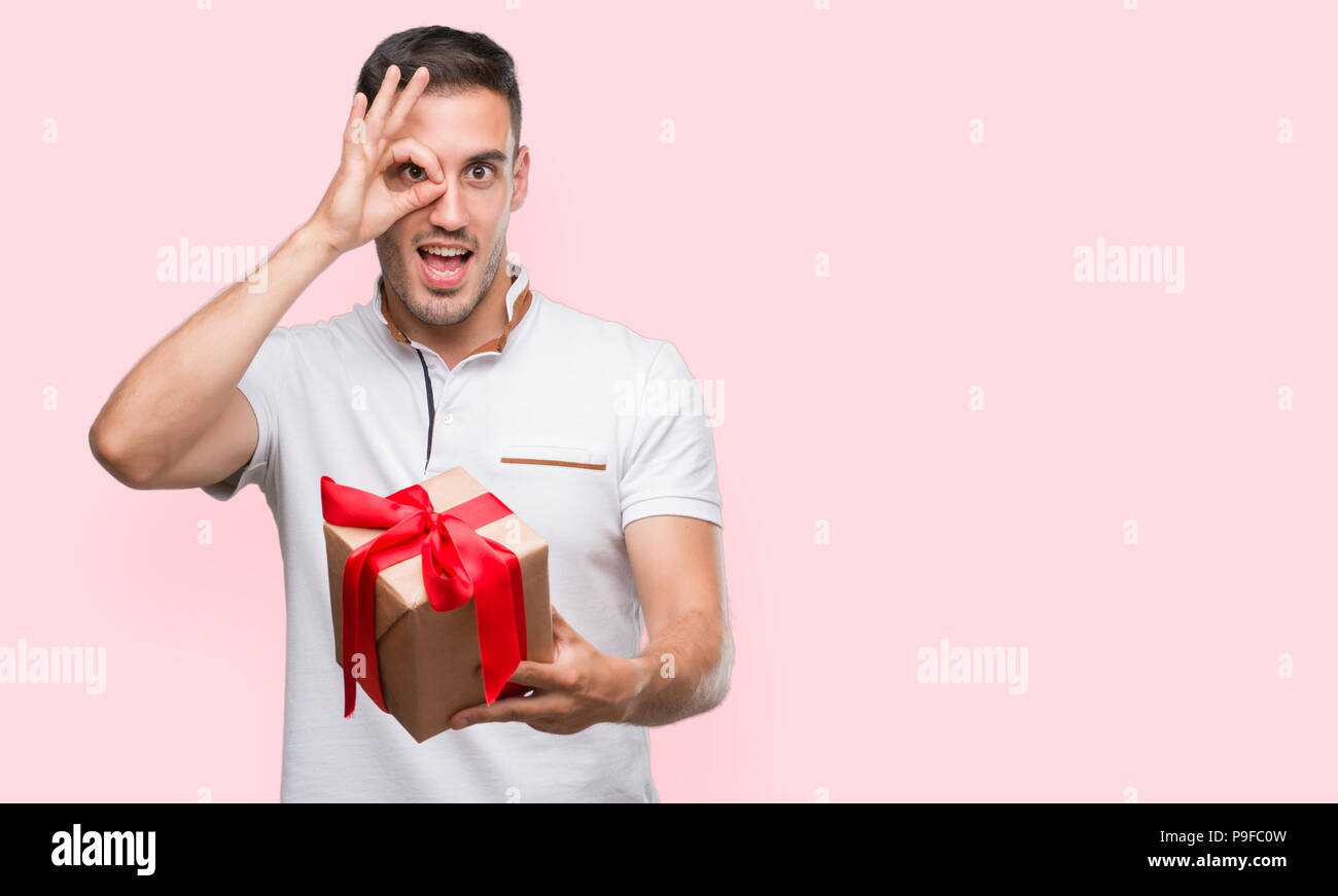 Handsome young man giving a present with happy face smiling doing ok ...