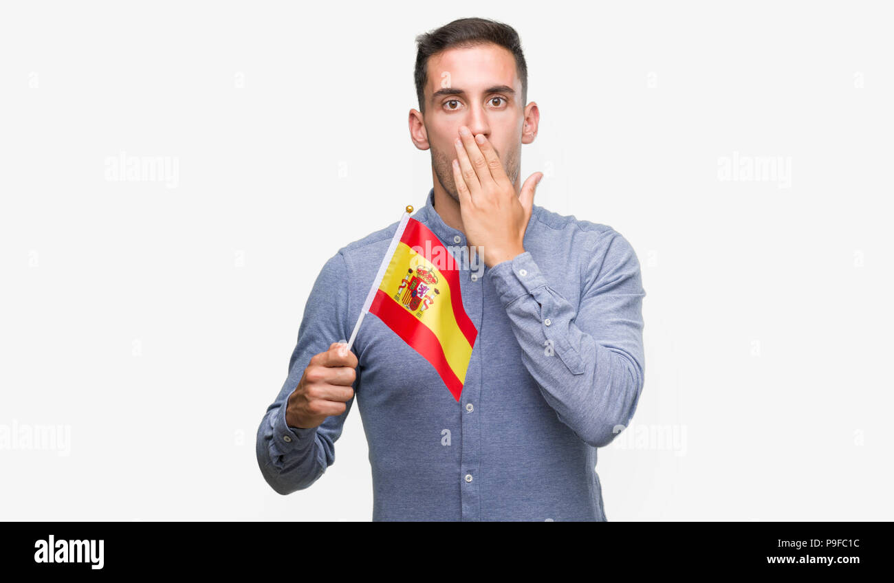 Handsome young man holding a flag of Spain cover mouth with hand ...