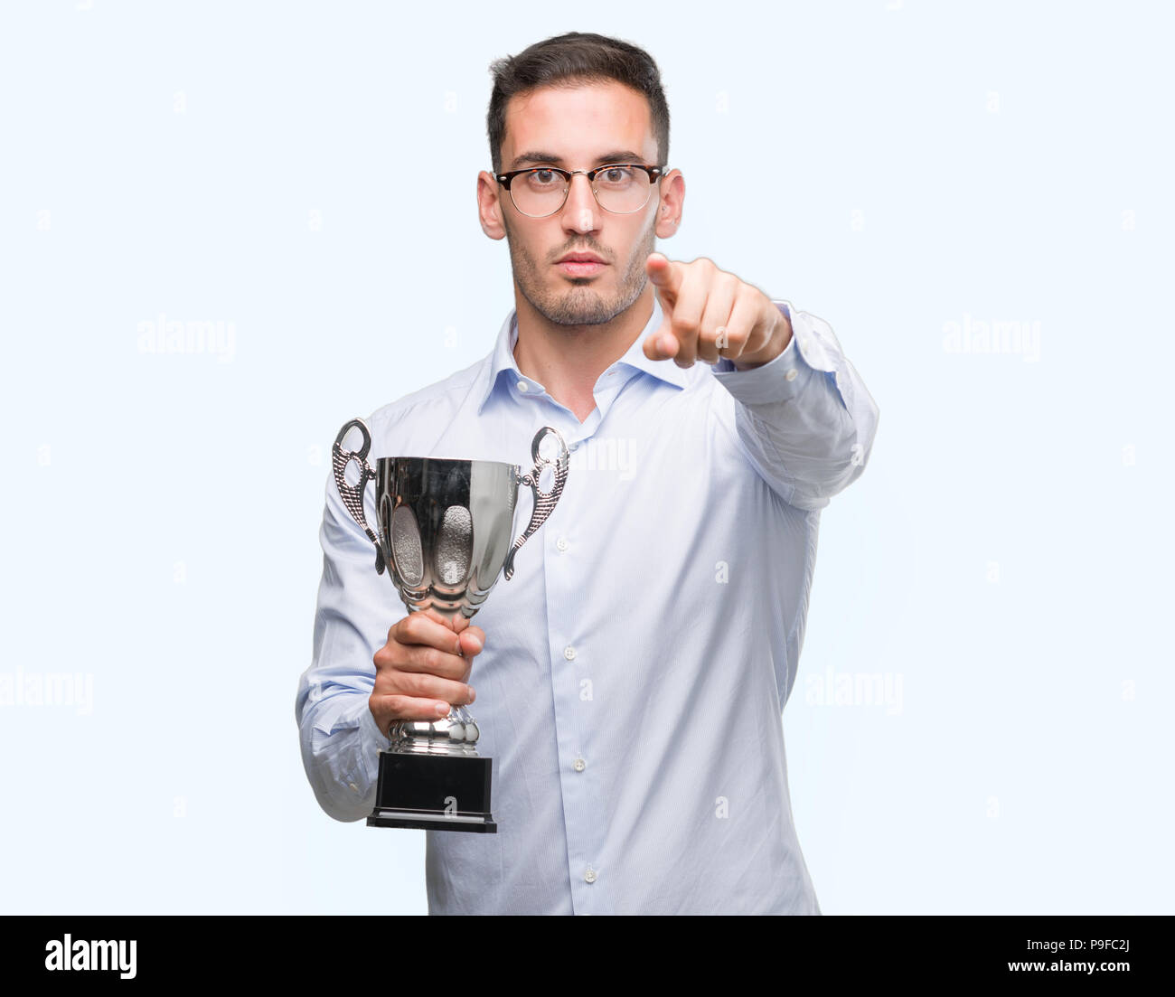Handsome young man holding trophy pointing with finger to the camera ...