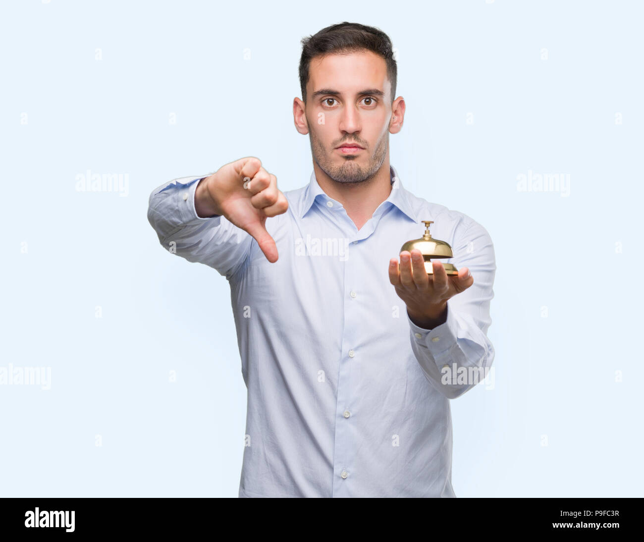 Handsome young man holding hotel ring bell with angry face, negative ...