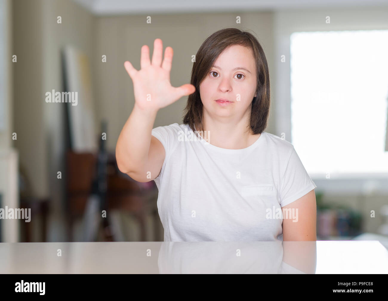 Down syndrome woman at home with open hand doing stop sign with serious ...