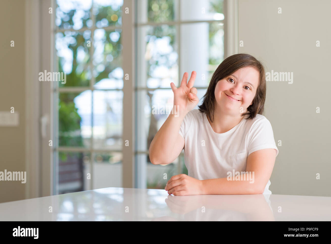 Down syndrome woman at home showing and pointing up with fingers number ...