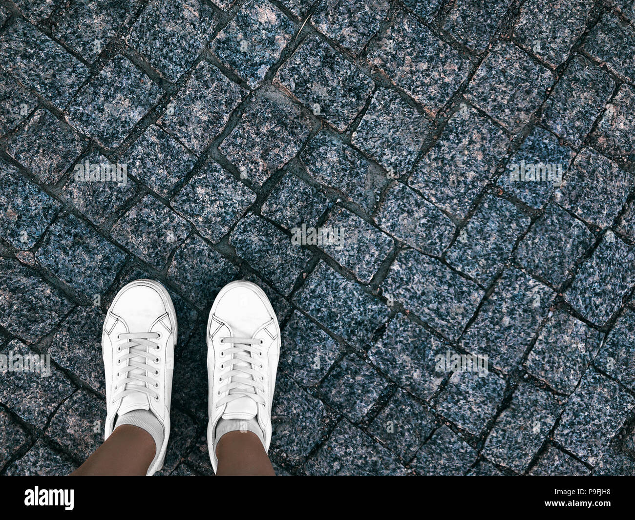 Female feet Top view Girl in white sneakers is standing on paving ...