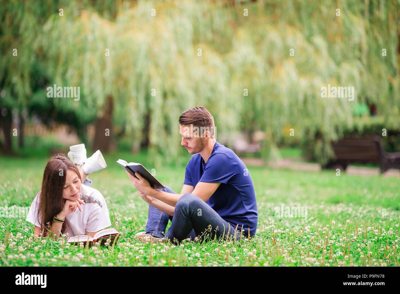 Relaxed young couple reading books while lying on grass Stock Photo - Alamy
