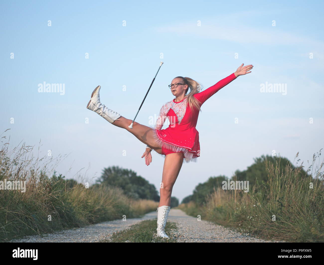 Bespectacled Blonde Teen Majorette Girl Twirling Baton Outdoors in Red ...