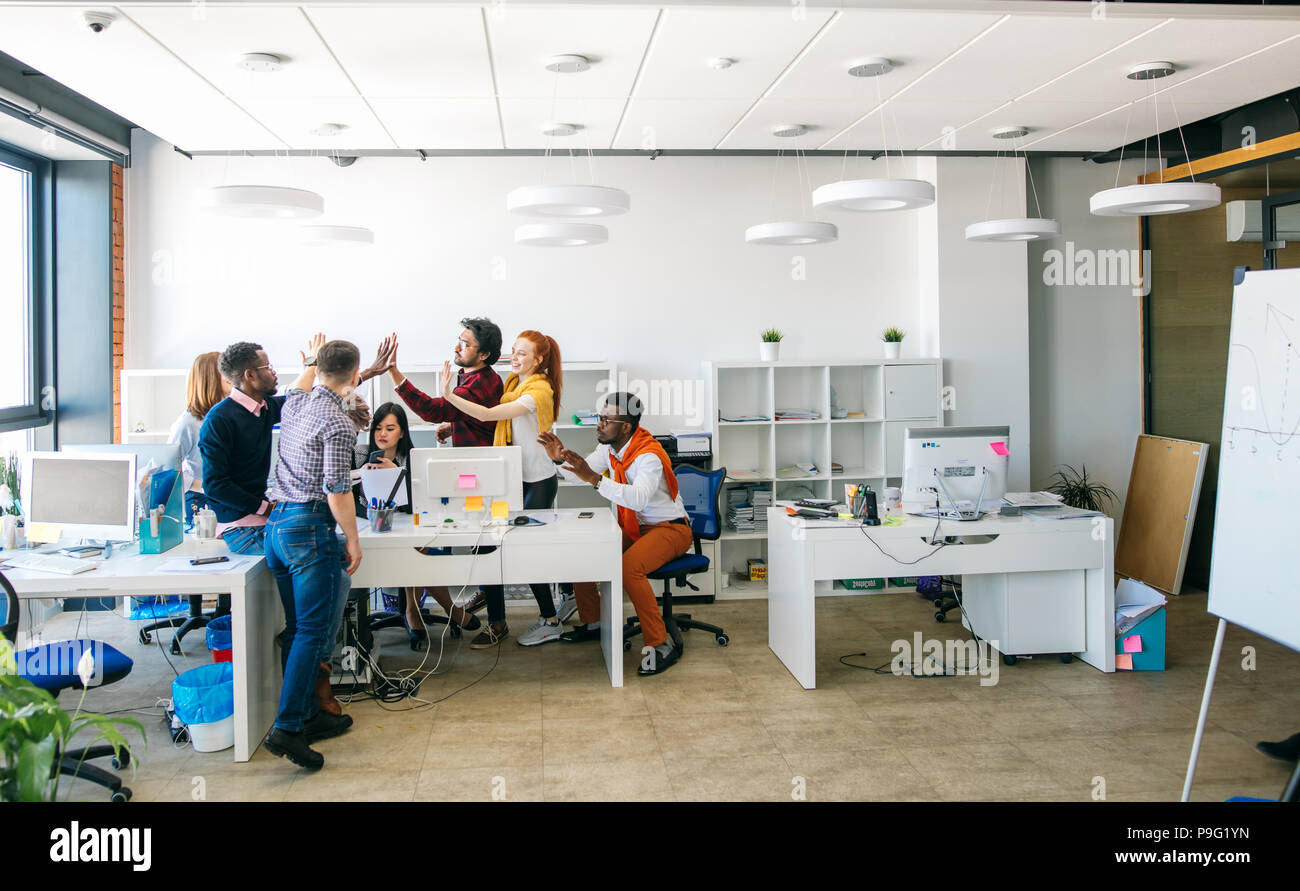 open plan room with mixed race energetic students giving high five to ...