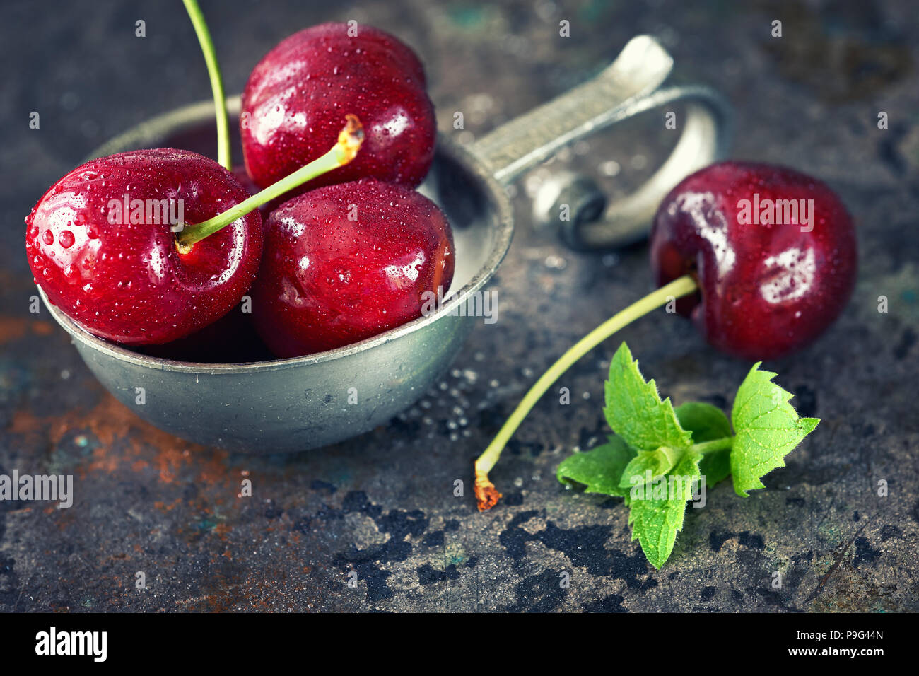 Close-up on dark cherries and fresh mint leaves in pewt spoon on dark ...