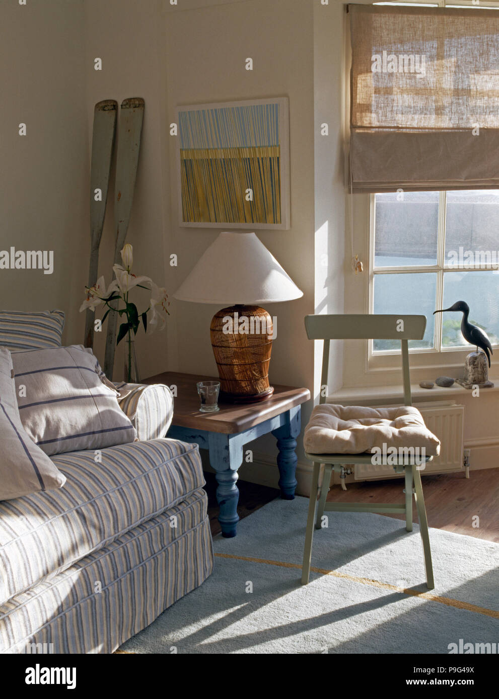 Oars in corner of coastal sitting room with a striped sofa beside a ...