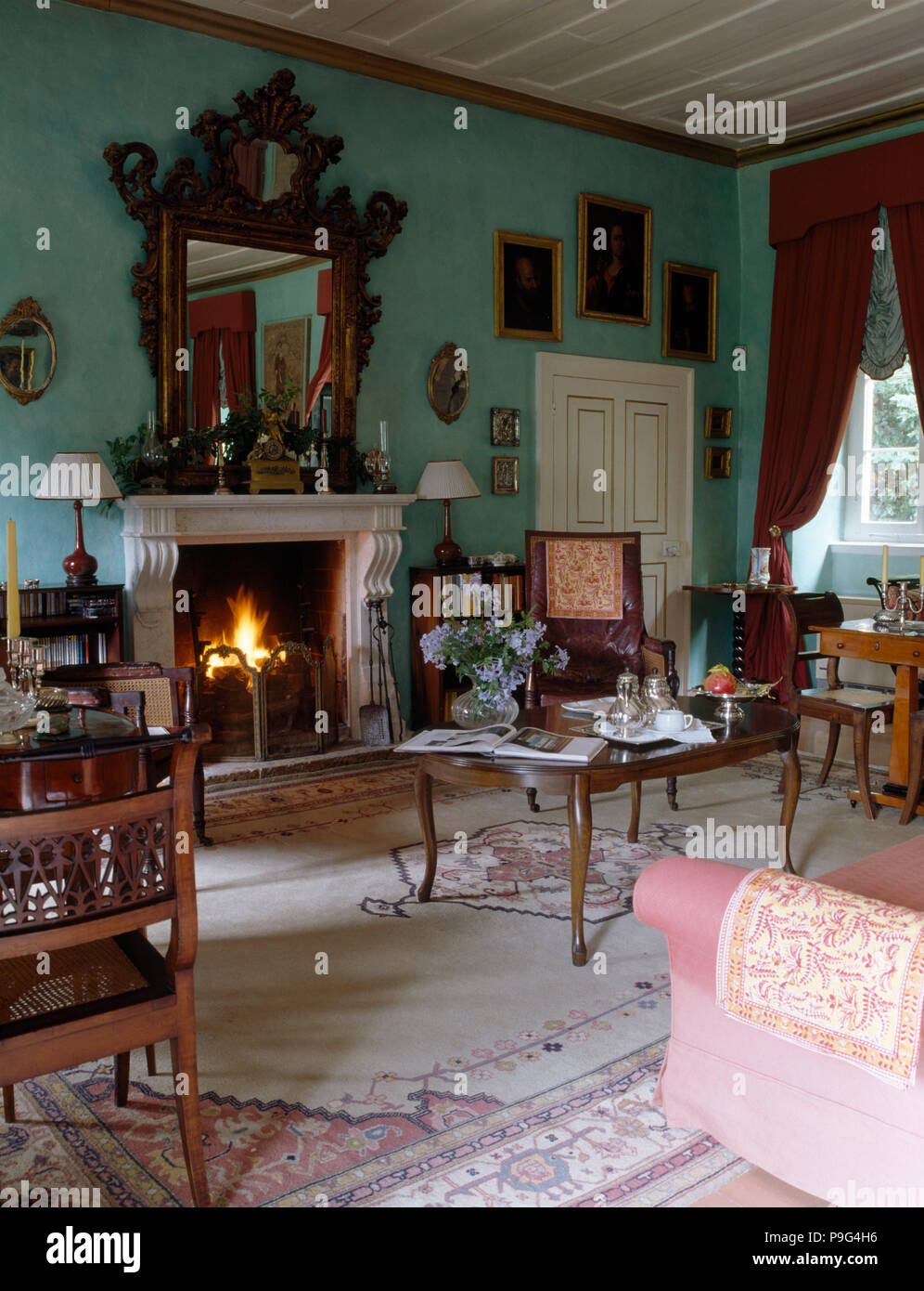 Lighted fire in fireplace in a turquoise country drawing room with ...