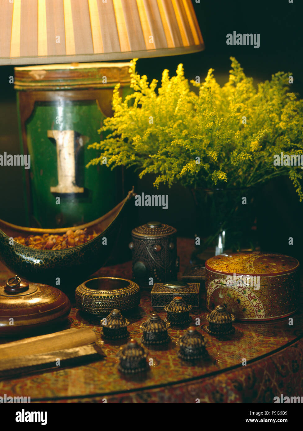 Yellow solidago in vase on table with collection of antique lacquered ...