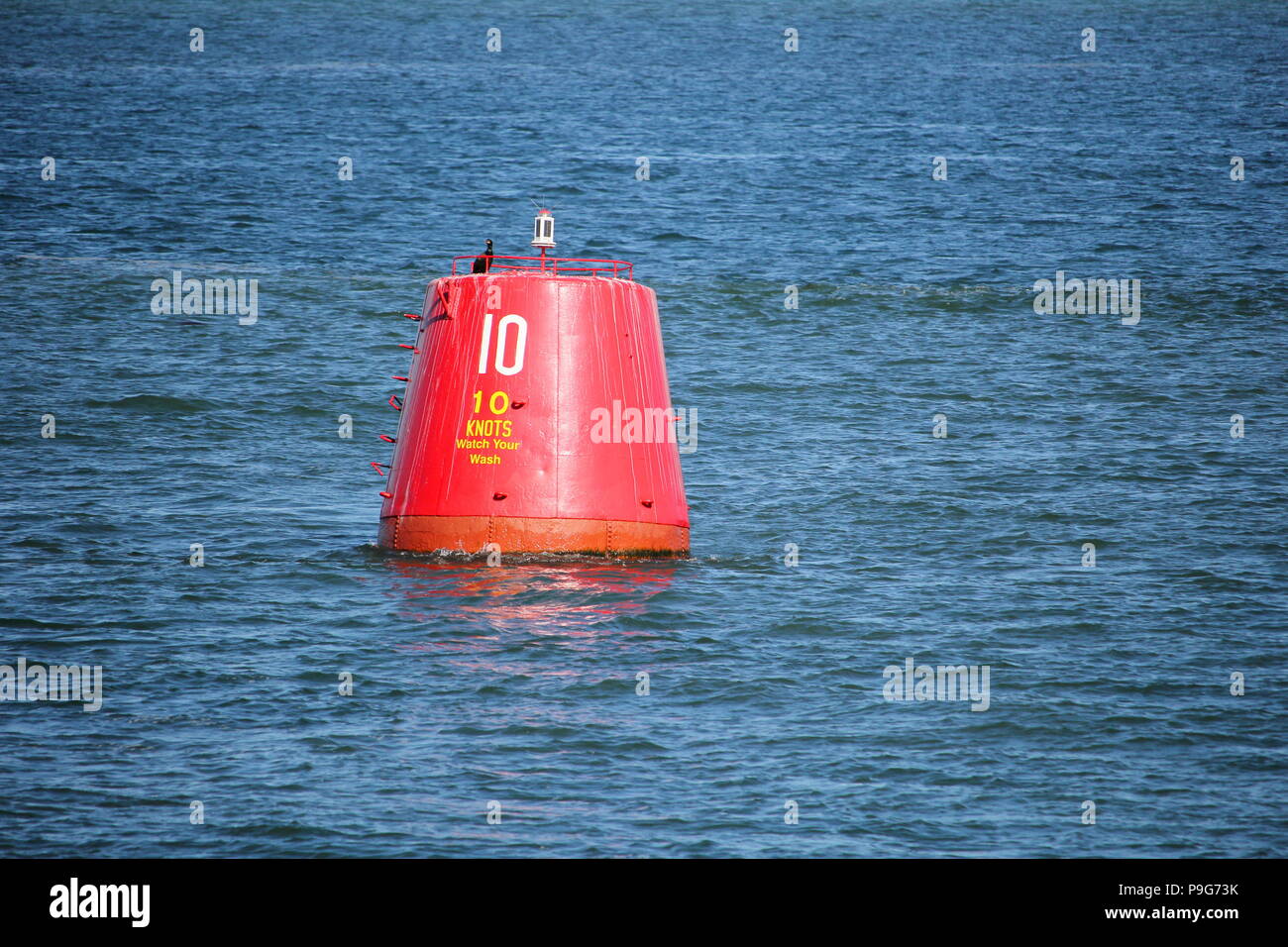 Red beacon buoy with speed limit of ten knots, floating in blue sea or ...