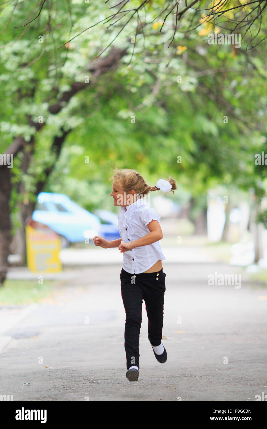little cute schoolgirl in school uniform runs outside, active childhood ...