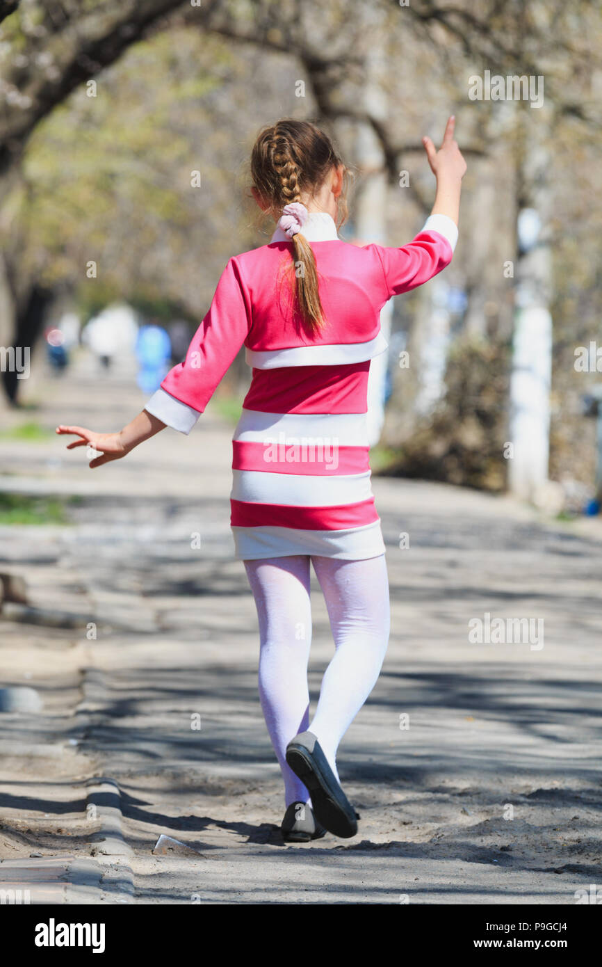 rear view of a little girl with braid in a pink dress dancing on the ...