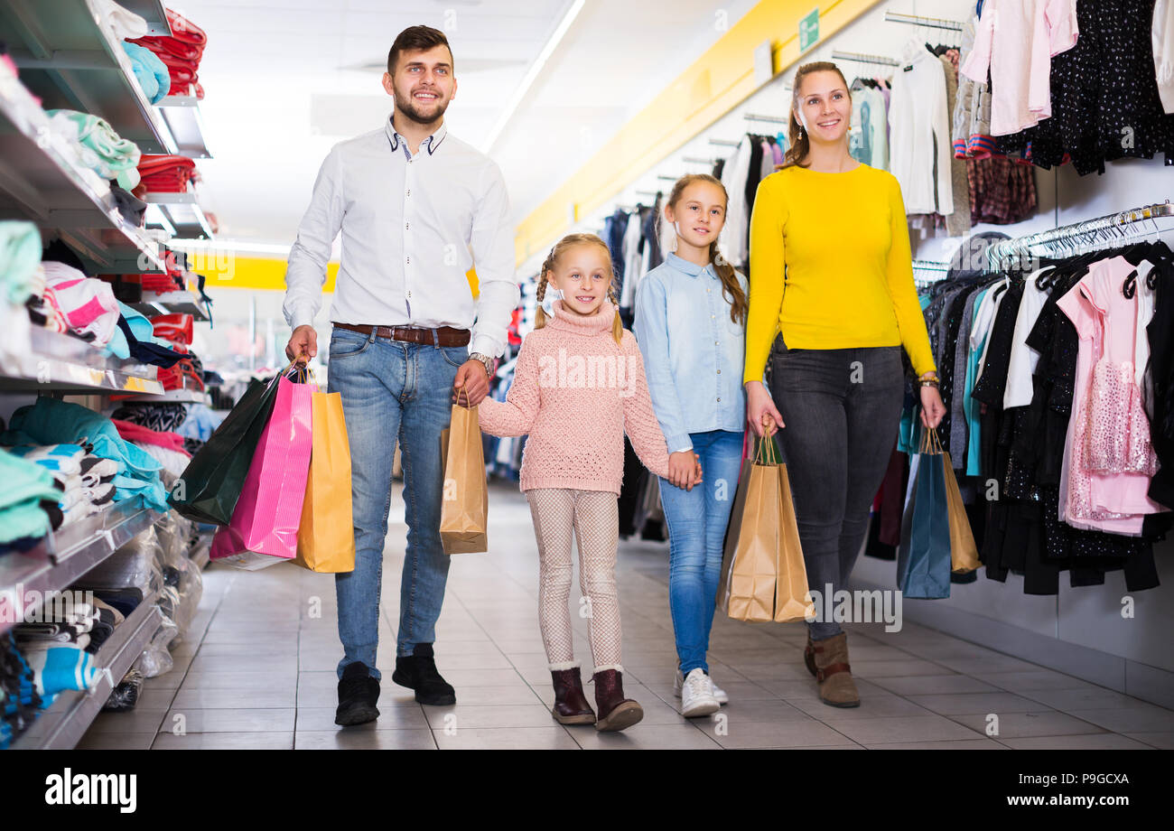 friendly family of four with shopping bags walking in clothing shop ...