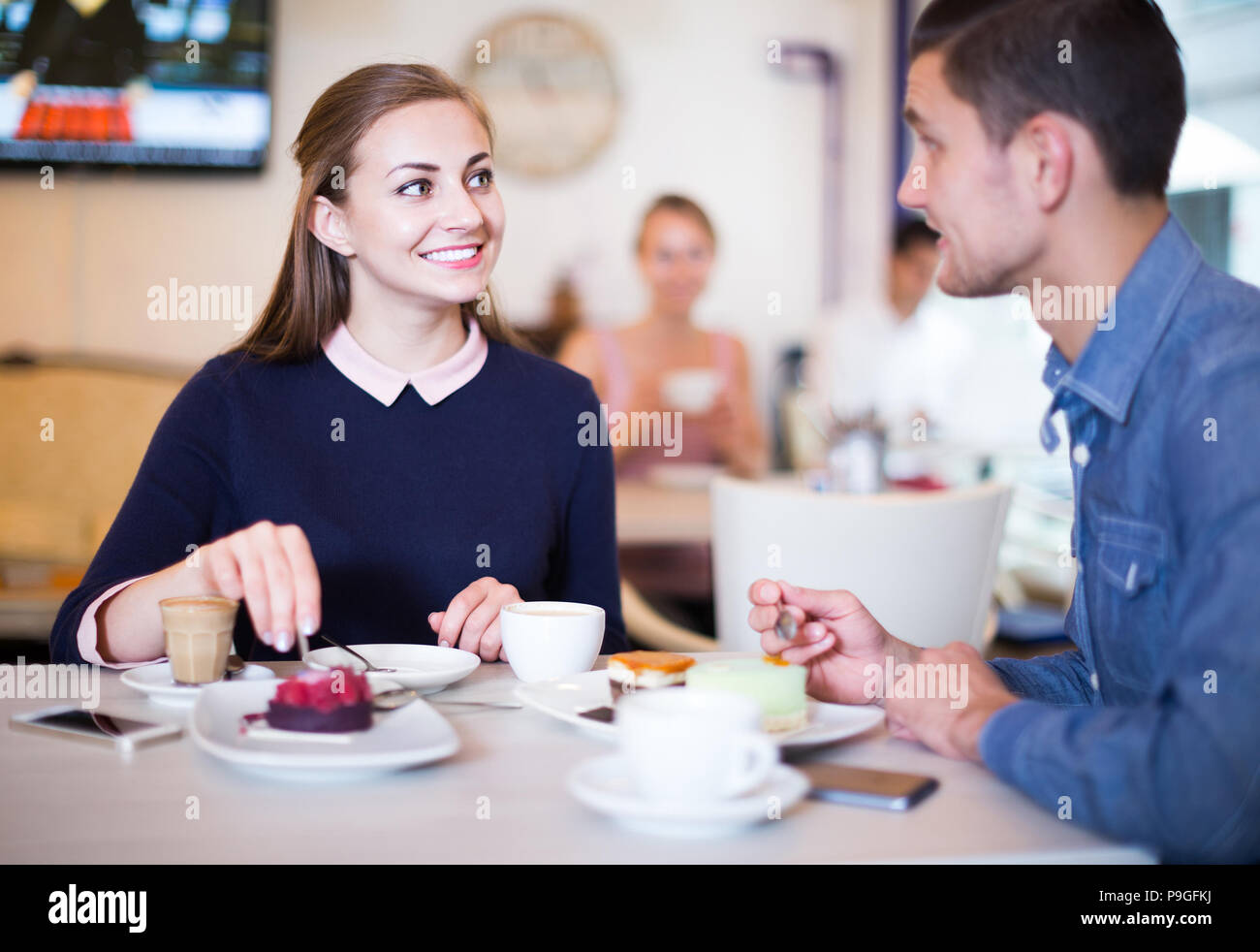 Smiling woman and boyfriend enjoying coffee with sweet dessert together ...